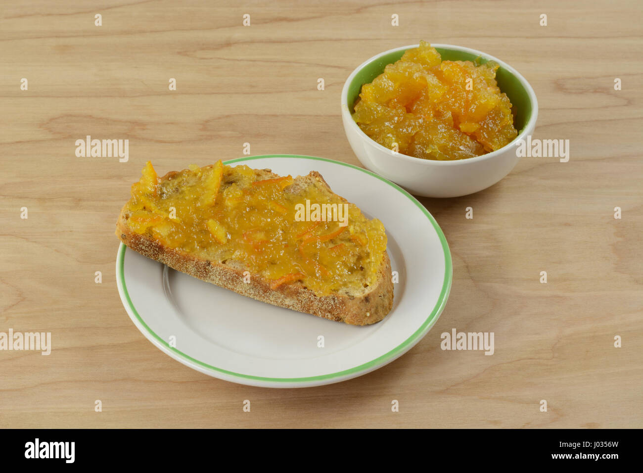 Orange marmalade in condiment bowl and on piece of wholegrain toast ...