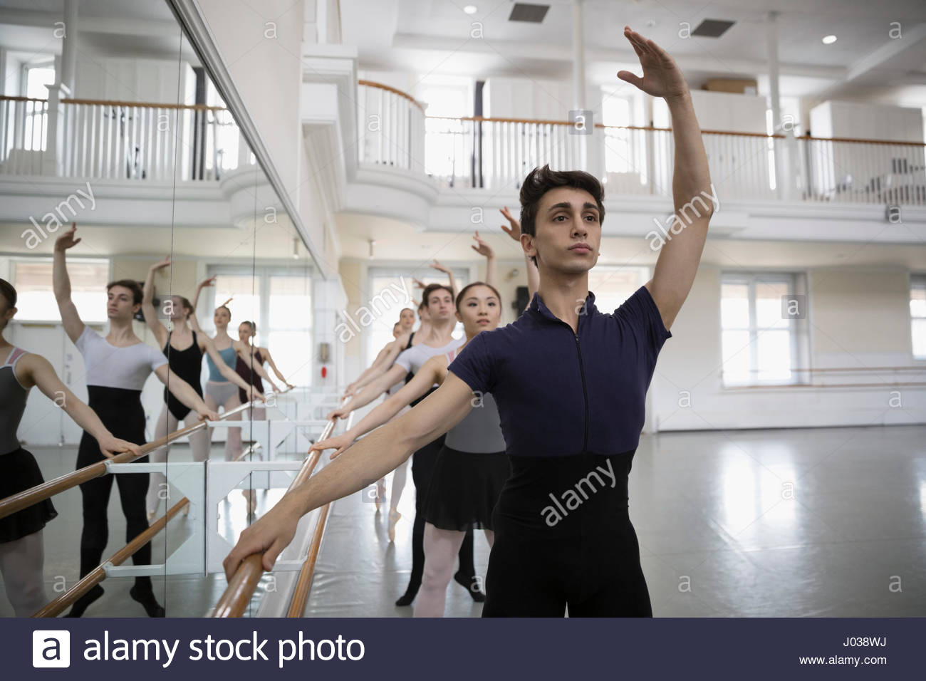 Focused ballet dancers practicing fourth position at barre in dance ...