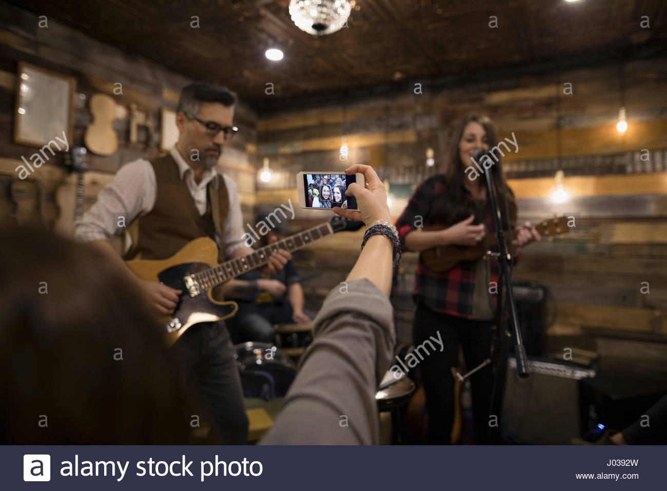 Woman in audience taking selfie behind musicians performing on garage ...