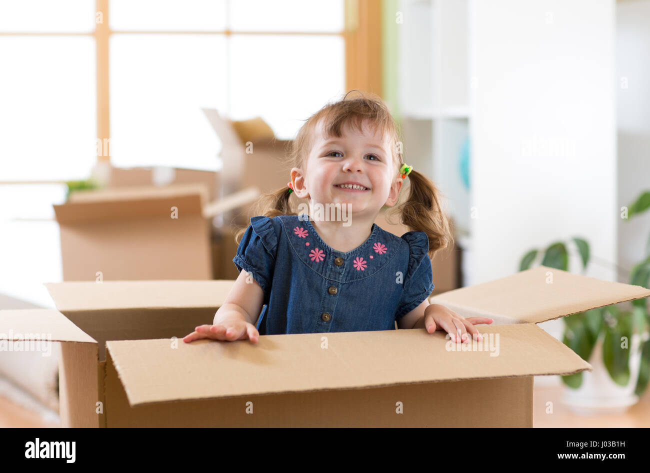 Laughing little girl sitting inside cardboard boxe in her new home ...