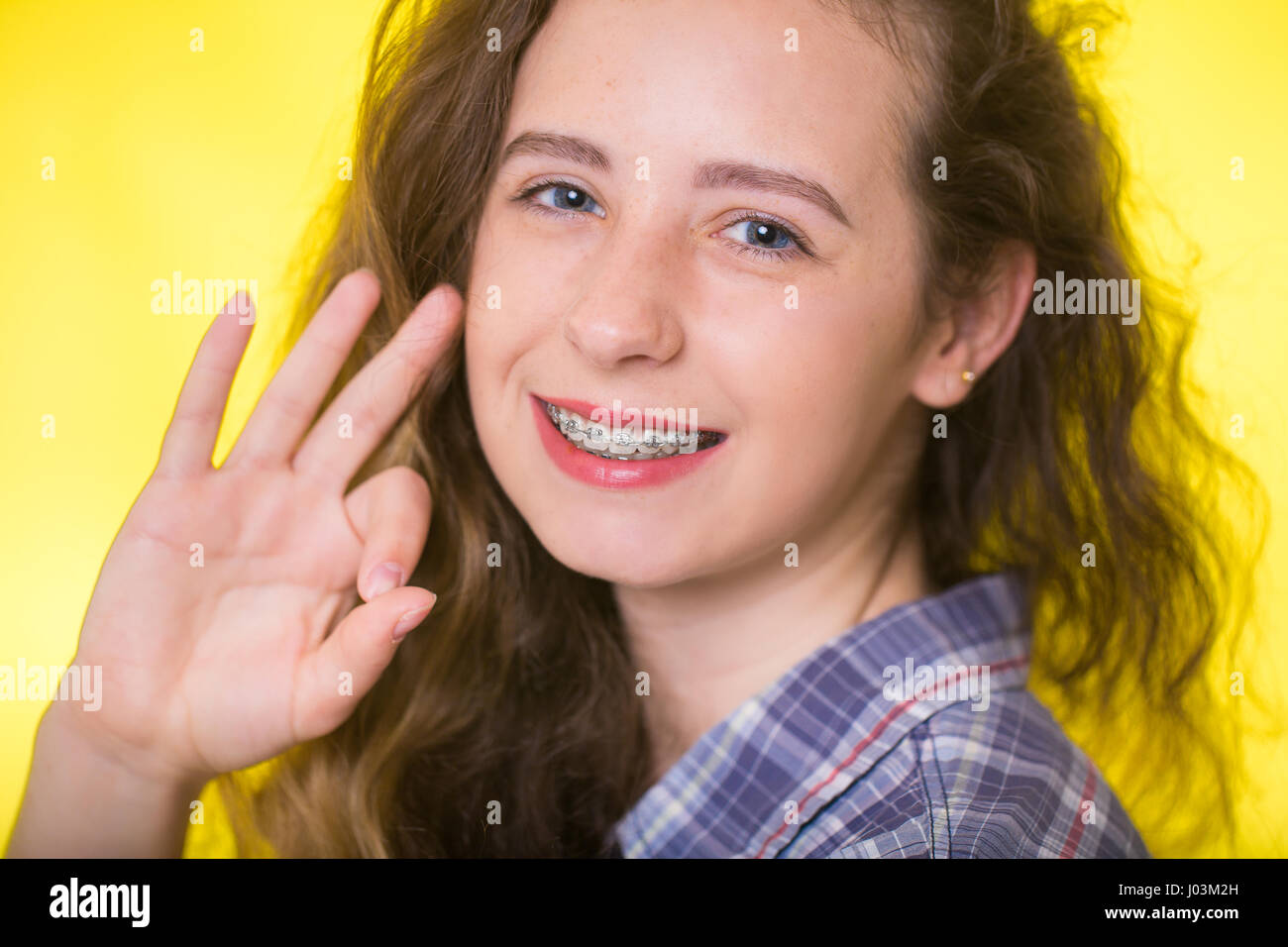 Young girl in a plaid shirt on yellow background showing her dental ...