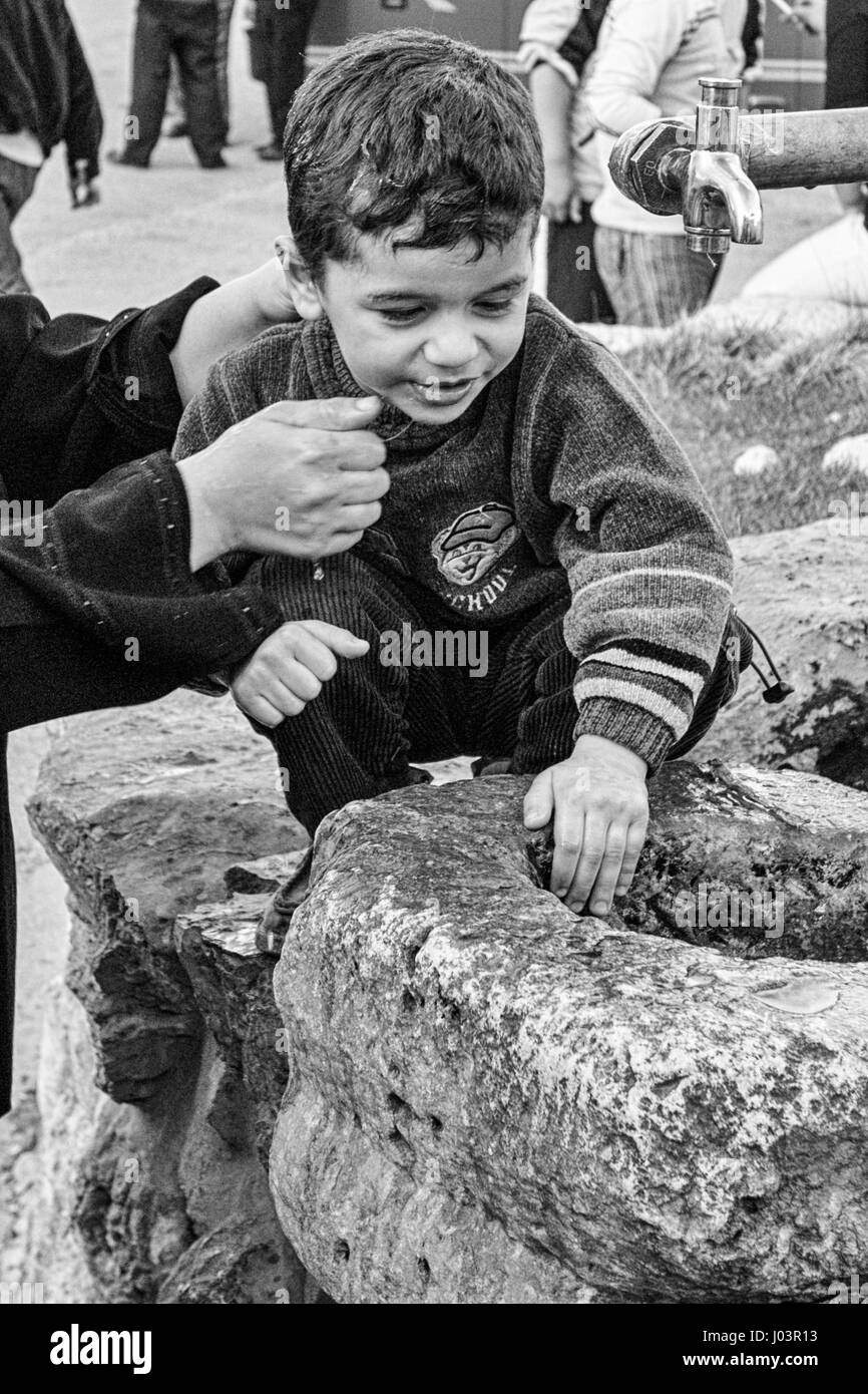 Syrian mother and son drink from the holy fountain at the Convent of ...
