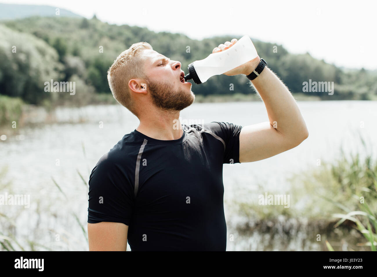 Side view of a thirsty male runner drinking water at a pond Stock Photo ...