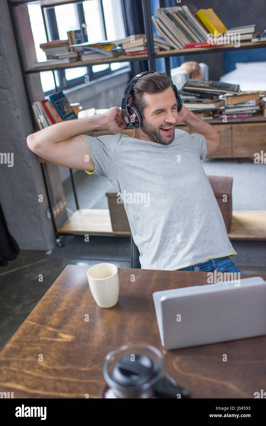 Young man in headphones yawning and stretching while using laptop Stock ...