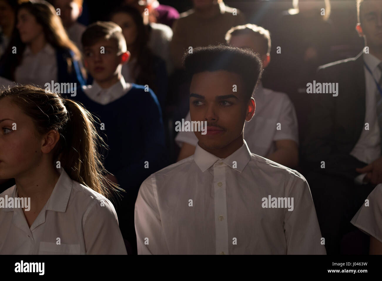 Crowd of teenage students in a lecture hall. They are looking towards ...