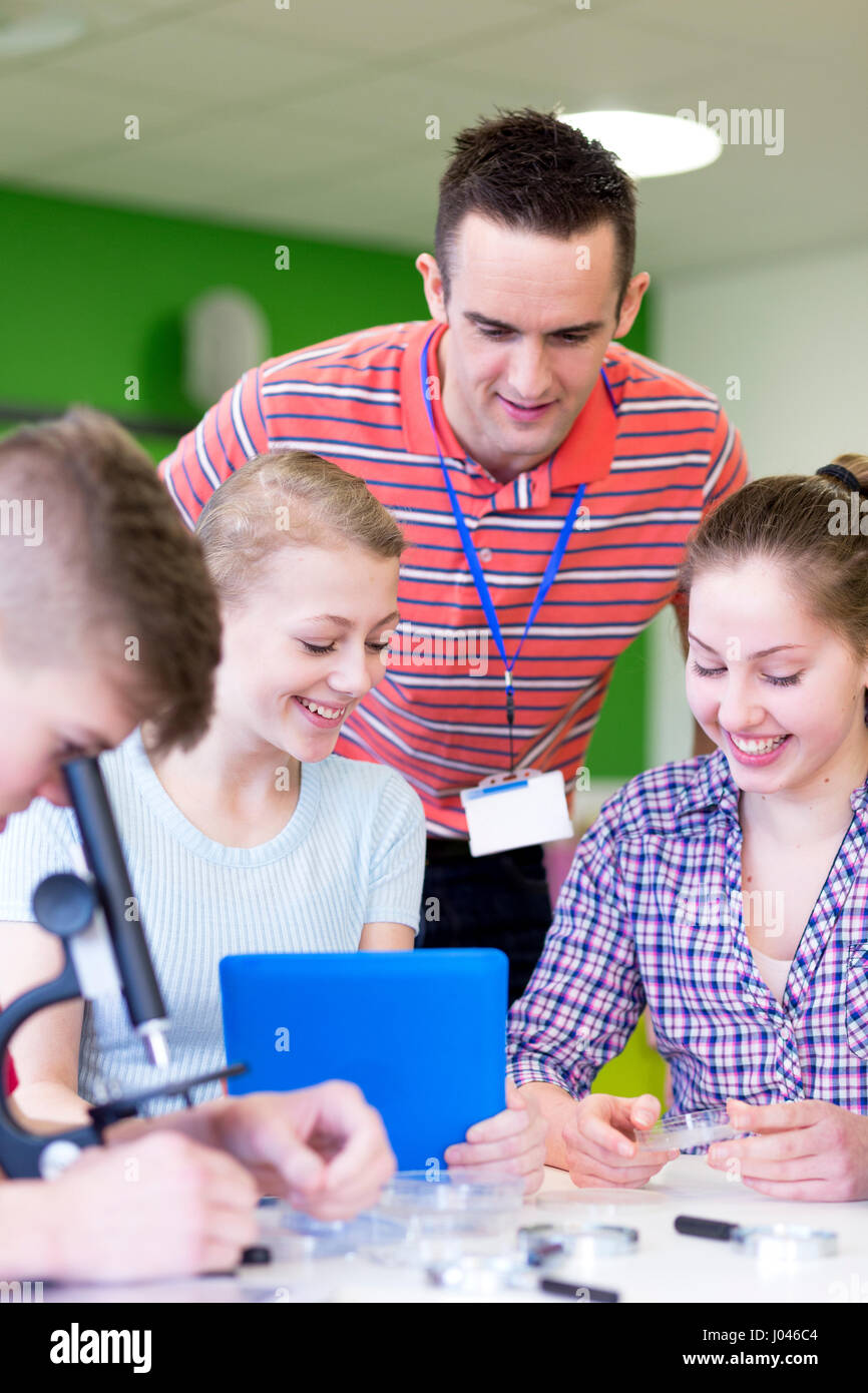 Teacher is supervising his students as they experiment with microscopes ...