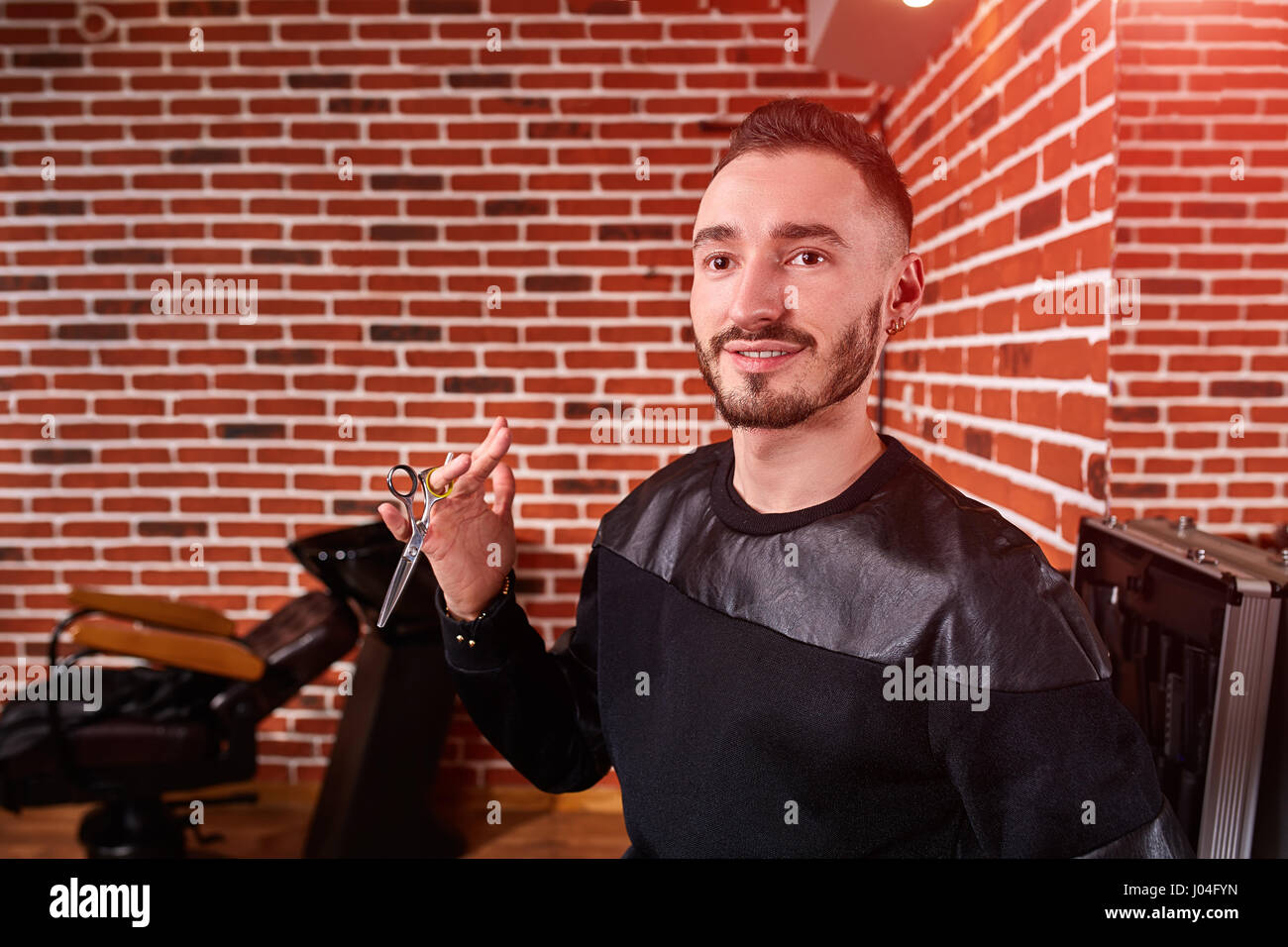 Portrait of successful male barber with scissors while looking at ...