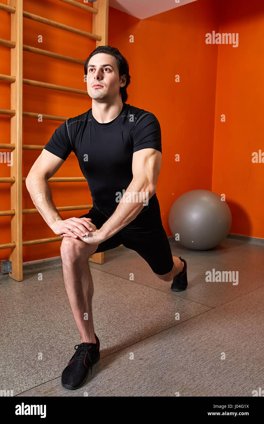 Strong man in the black sportwear stretching legs before gym workout ...