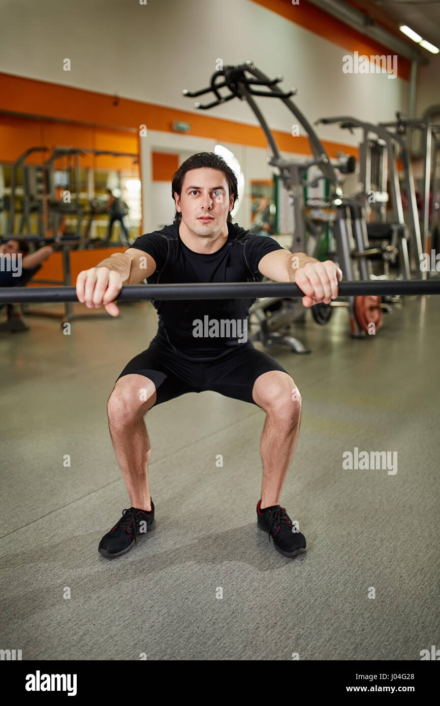 Young athletic man in black sportwear with bar of barbell flexing ...