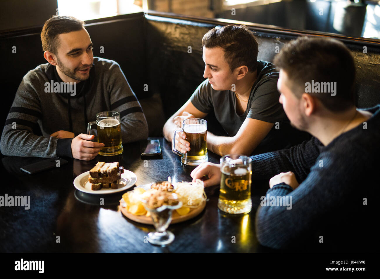 . Handsome young man toasting with beer and smiling while sitting with ...
