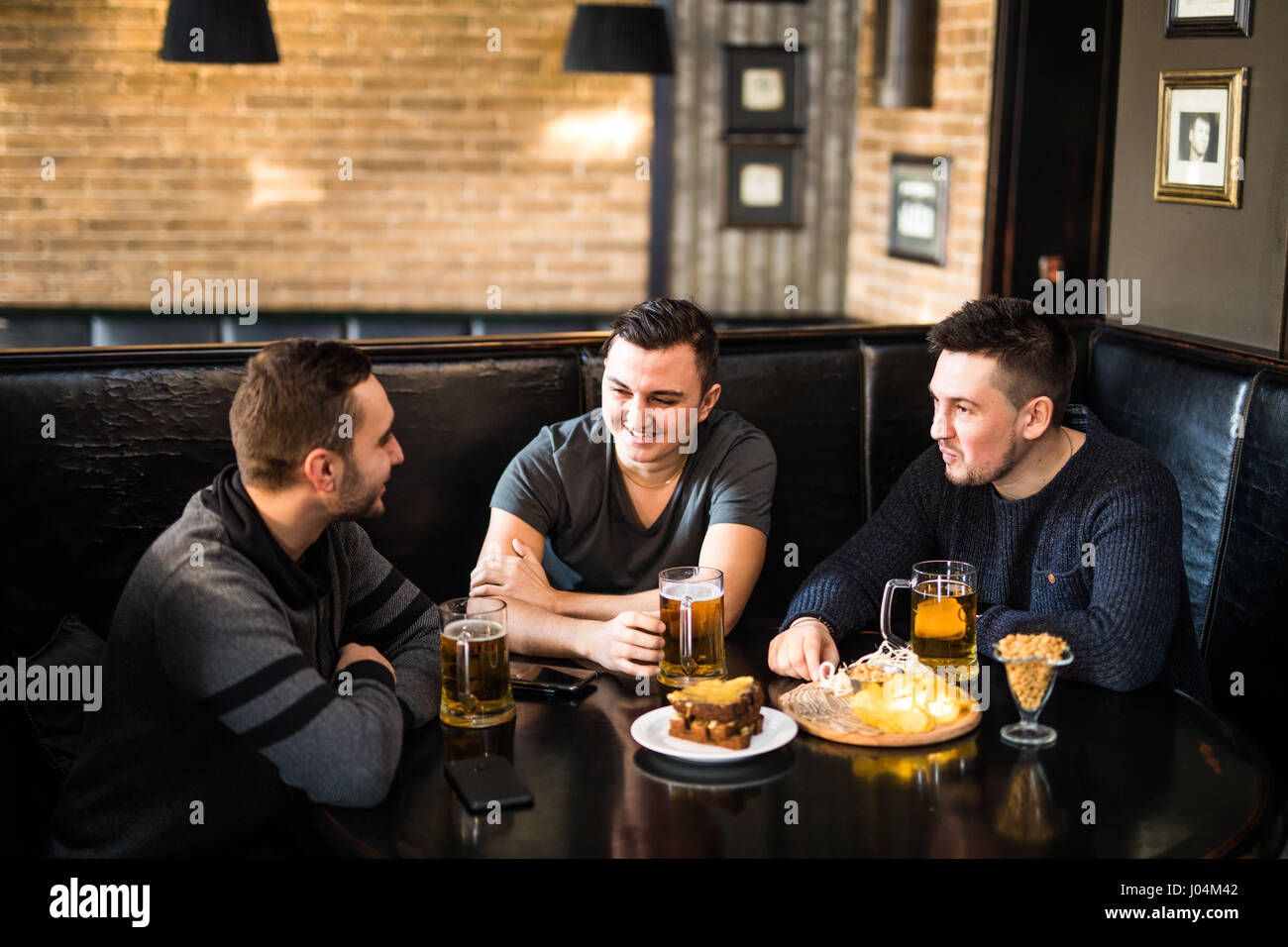 Meeting at the pub. Three happy friends drinking beer at the pub Stock ...