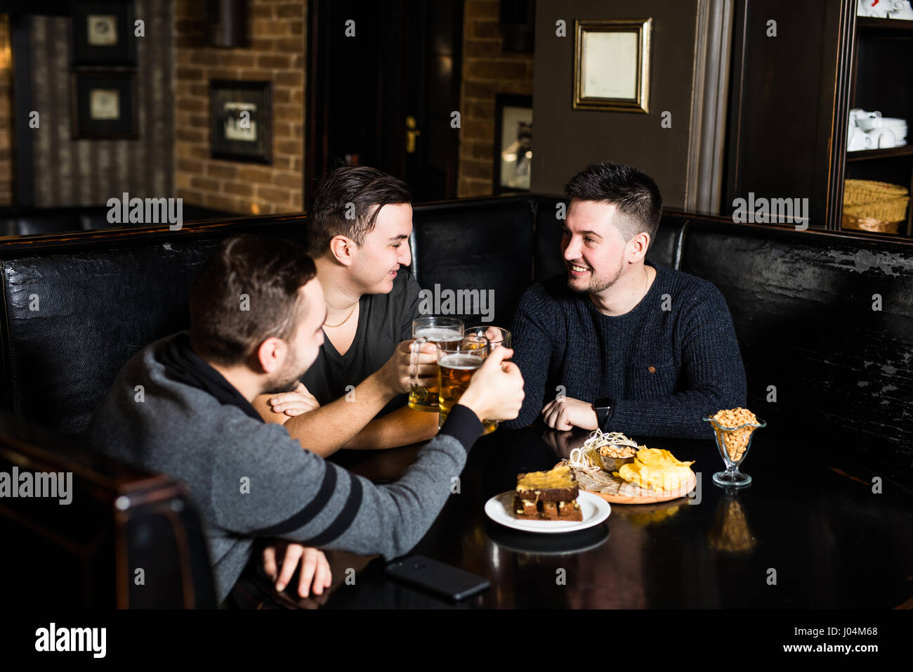 Three man friends drink beer and eat in traditional england pub. Meet ...