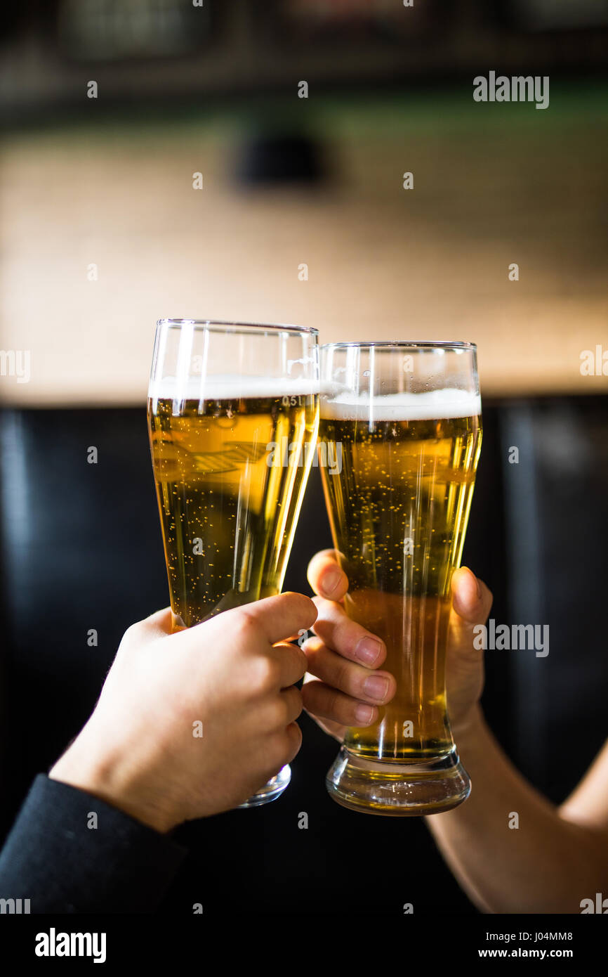 Close-up of two men in shirts toasting with beer at the bar counter ...