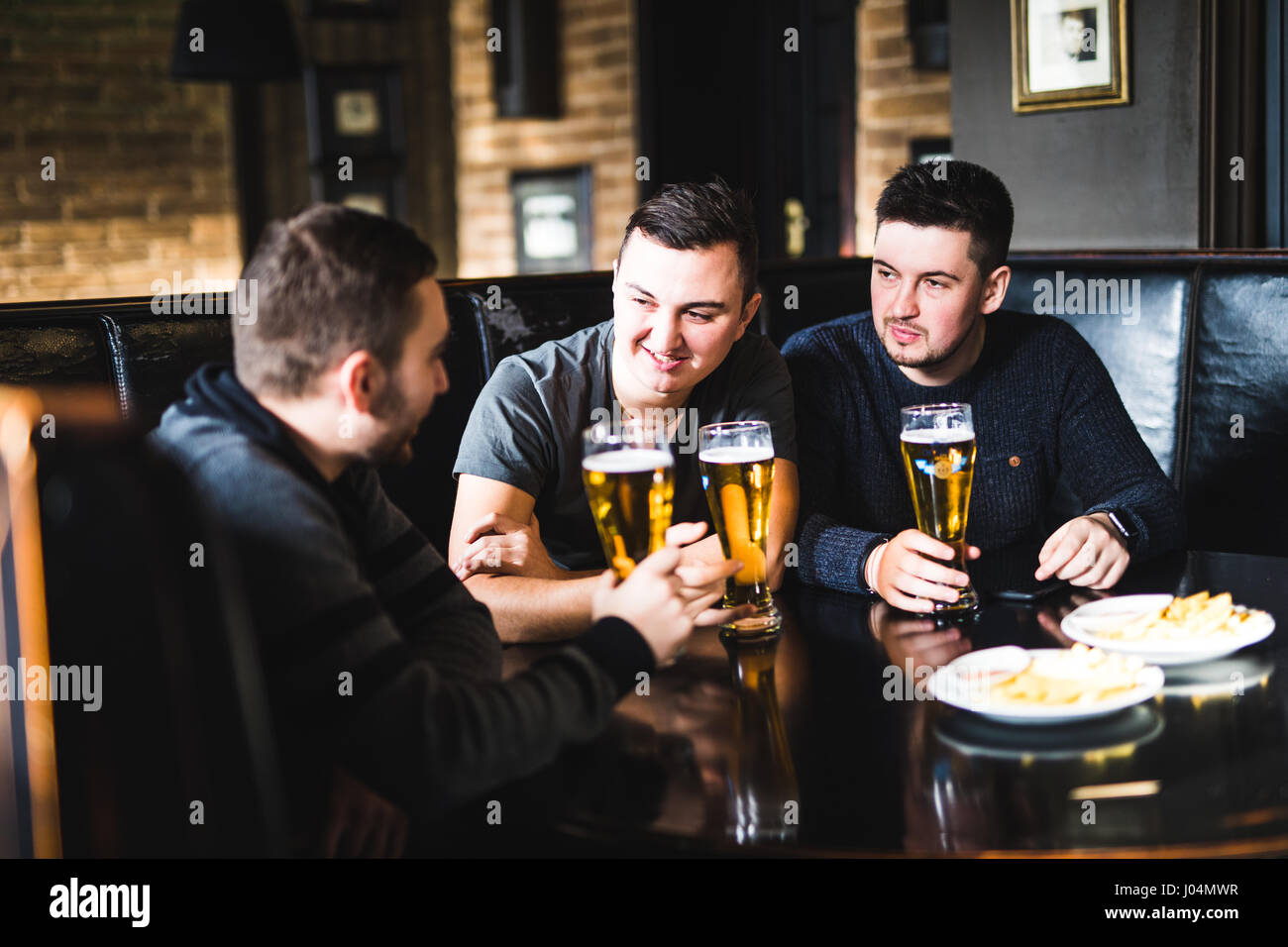 Three young men in casual clothes are talking, eating chips and ...
