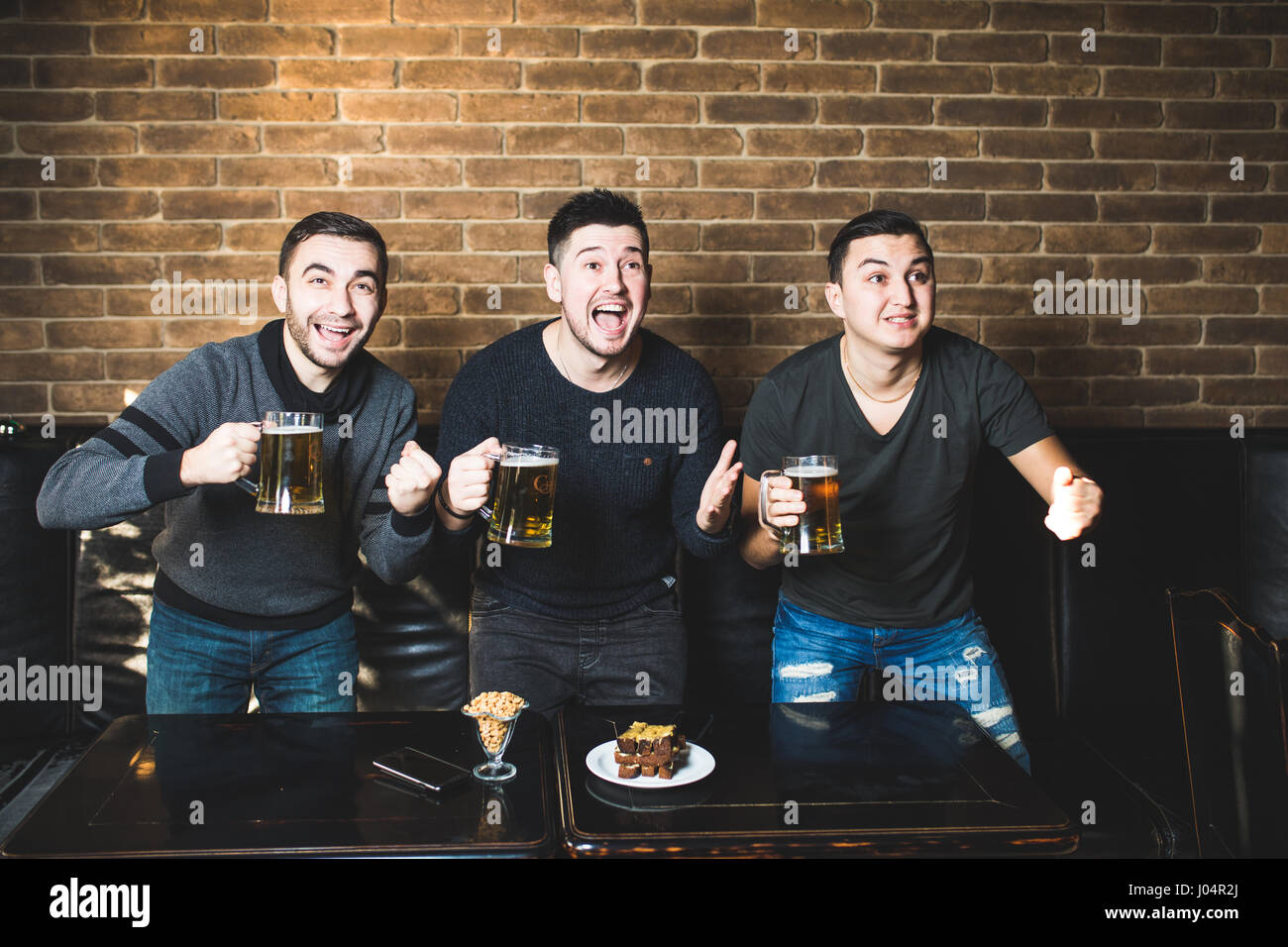 Three men with beer rejoice the victory of their favorite team in the ...