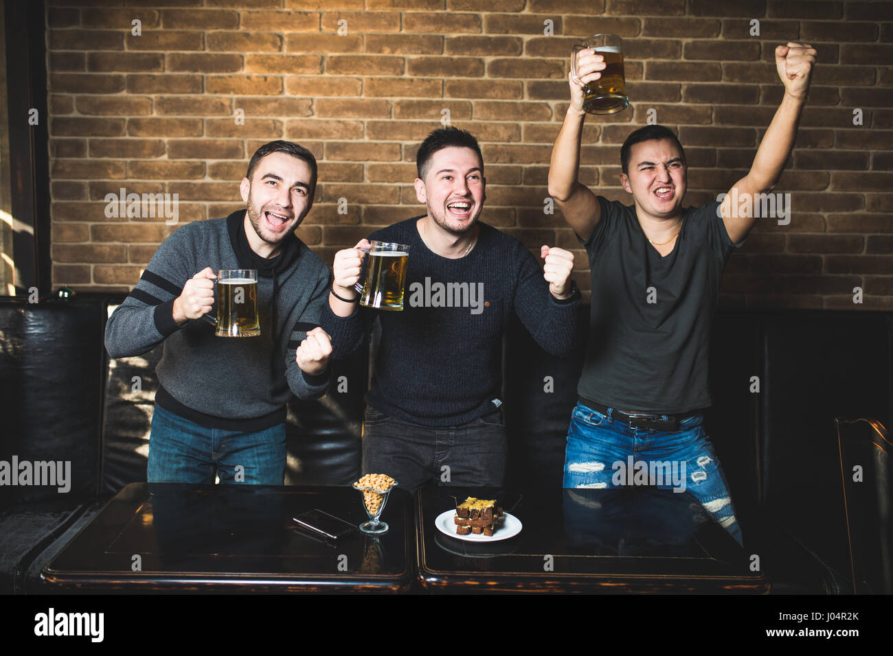 Three men with beer rejoice the victory of their favorite team in the ...