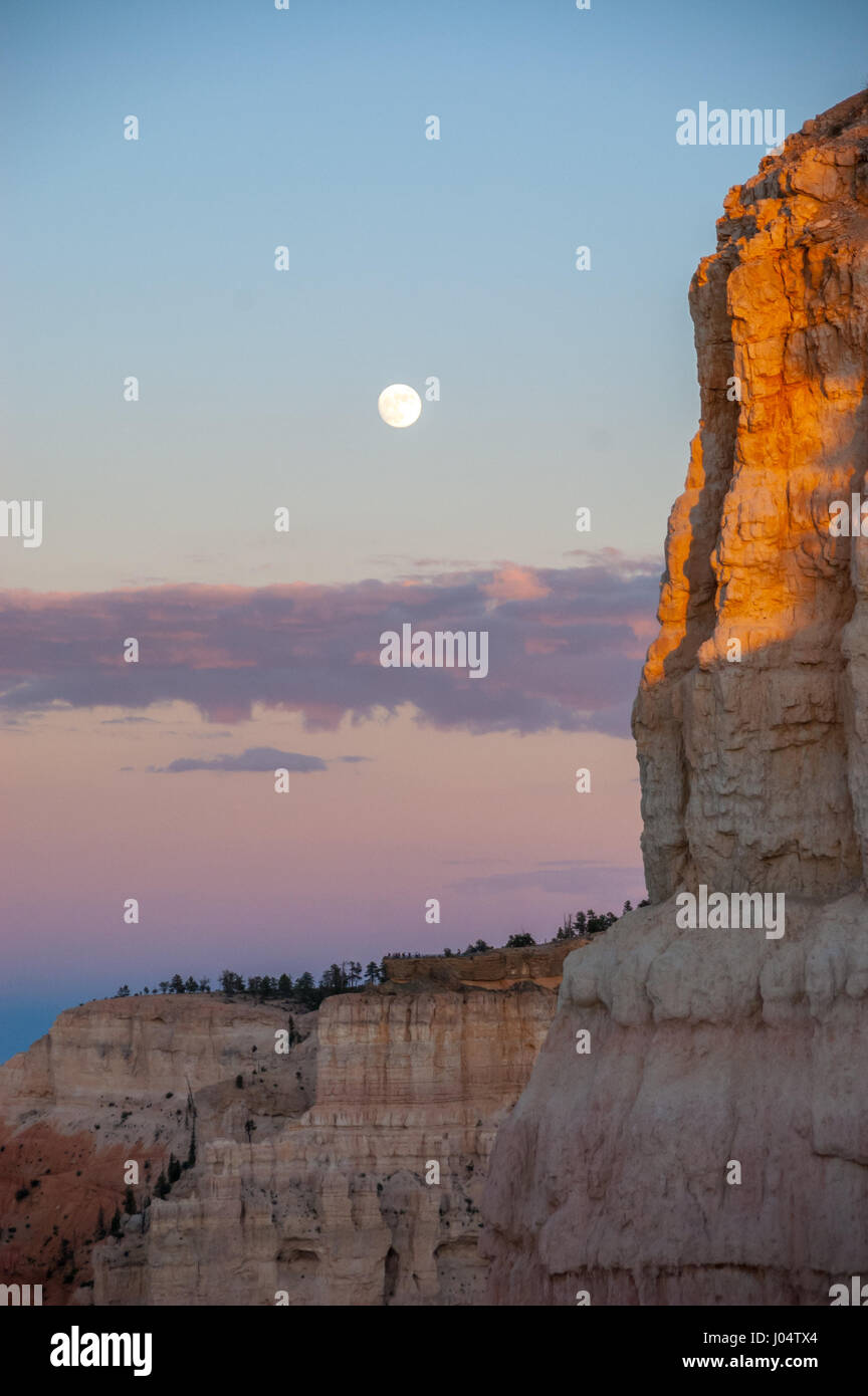 Full moon appears next to a vertical rock face colored rust by a ...