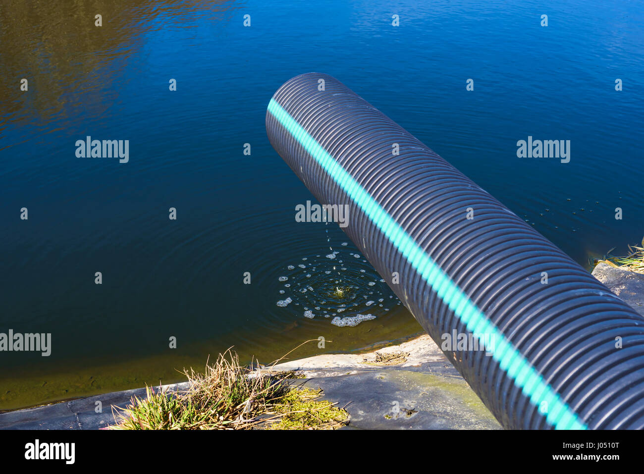 Landfill leachate pouring into pond from a black and blue pipe ...