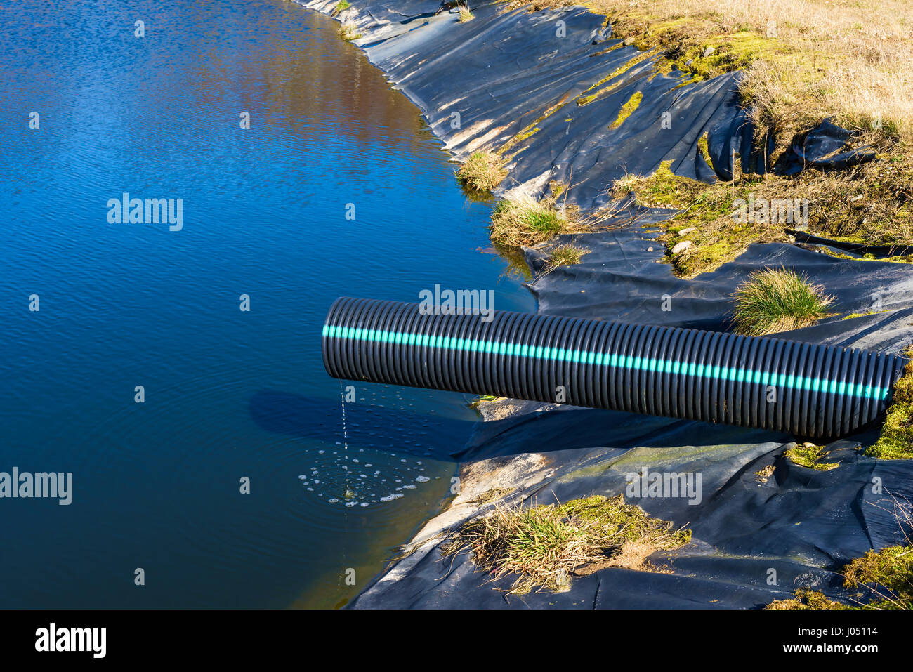 Landfill leachate pouring into pond from a black and blue pipe ...
