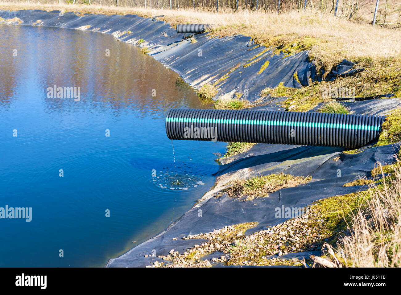 Landfill leachate pouring into pond from a black and blue pipe ...