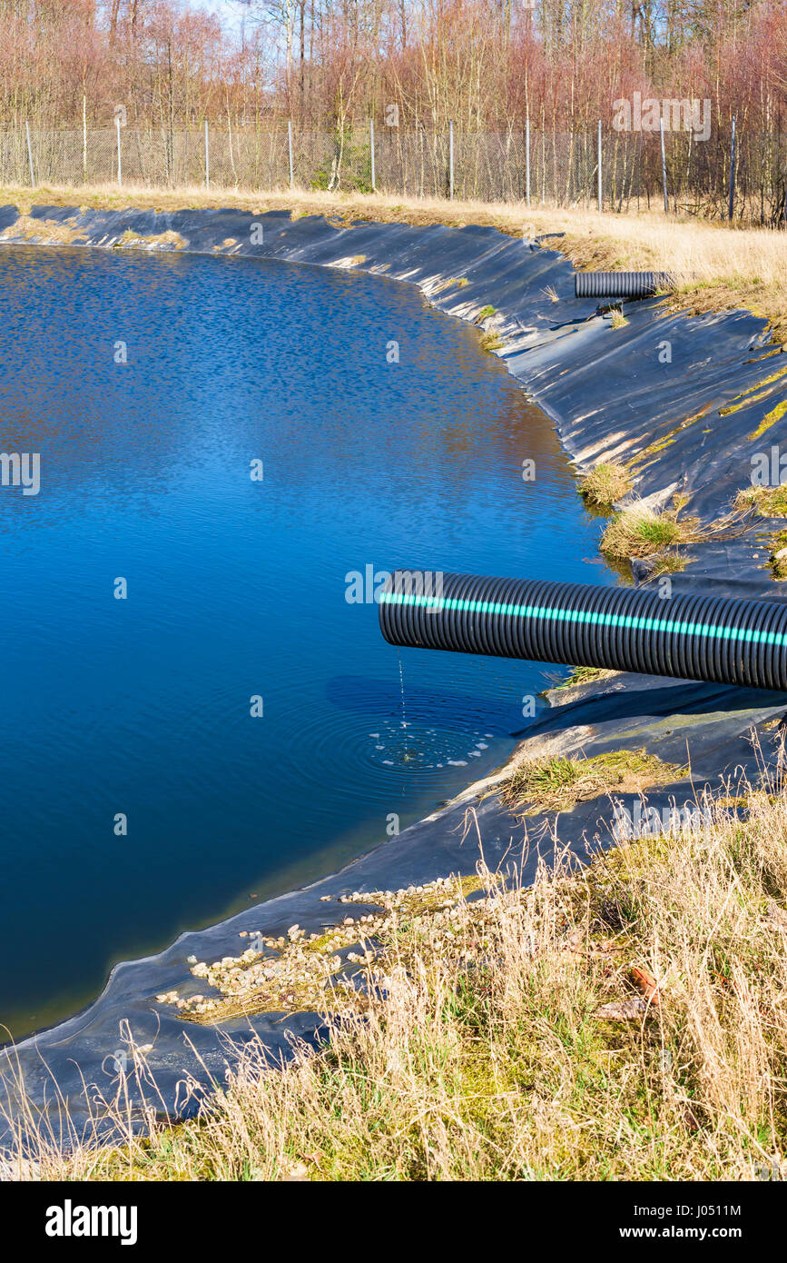 Landfill leachate pouring into pond from a black and blue pipe ...