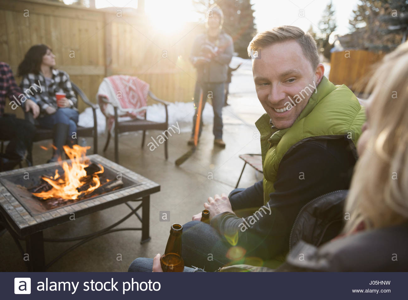Smiling couples drinking beer at fire pit in snowy driveway Stock Photo ...