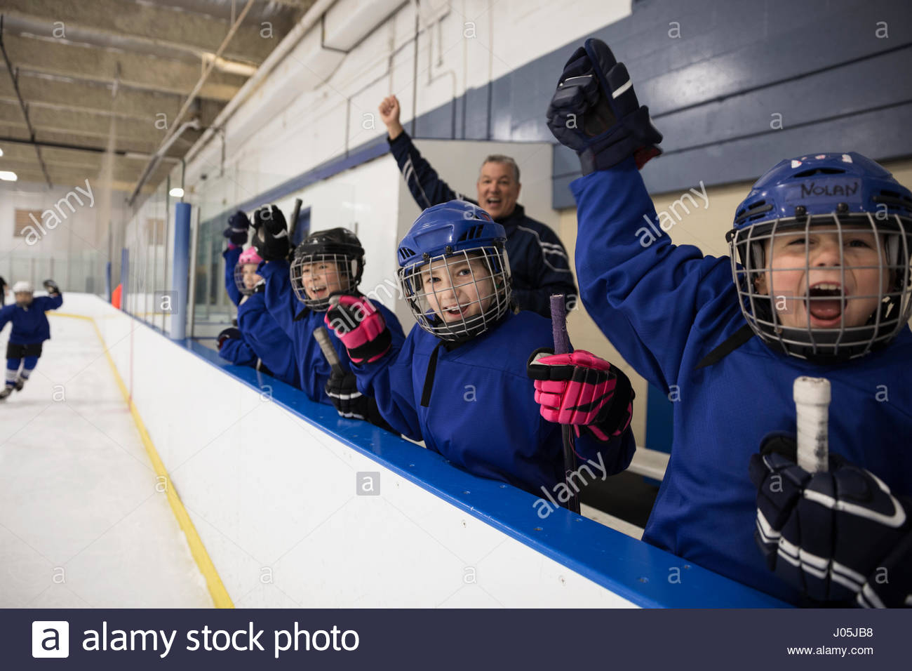 Boy and girl ice hockey players cheering, watching game from bench ...