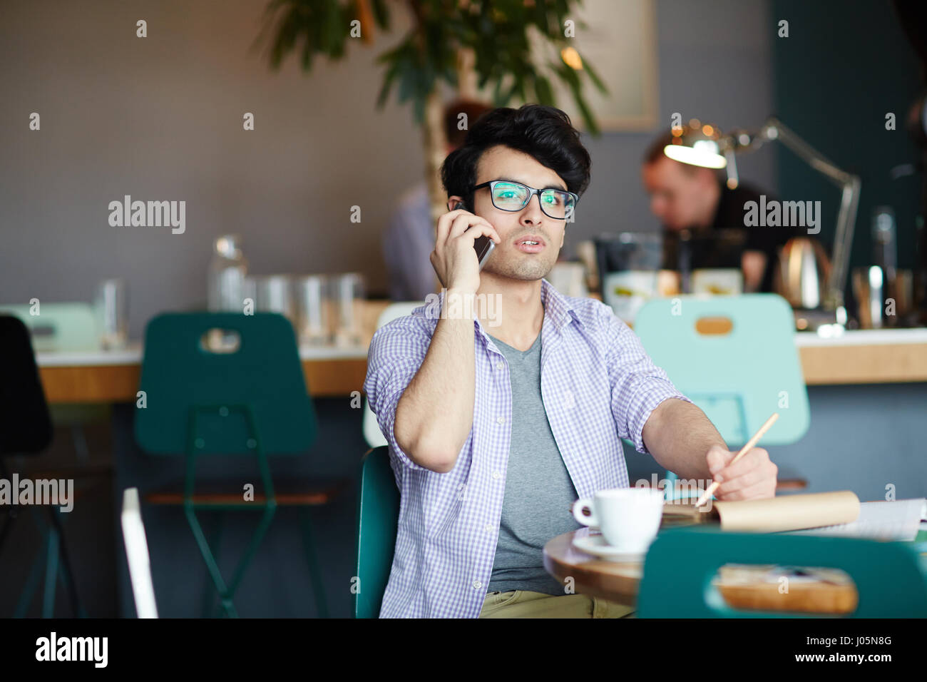 Portrait of young creative man calling by phone while making notes and ...