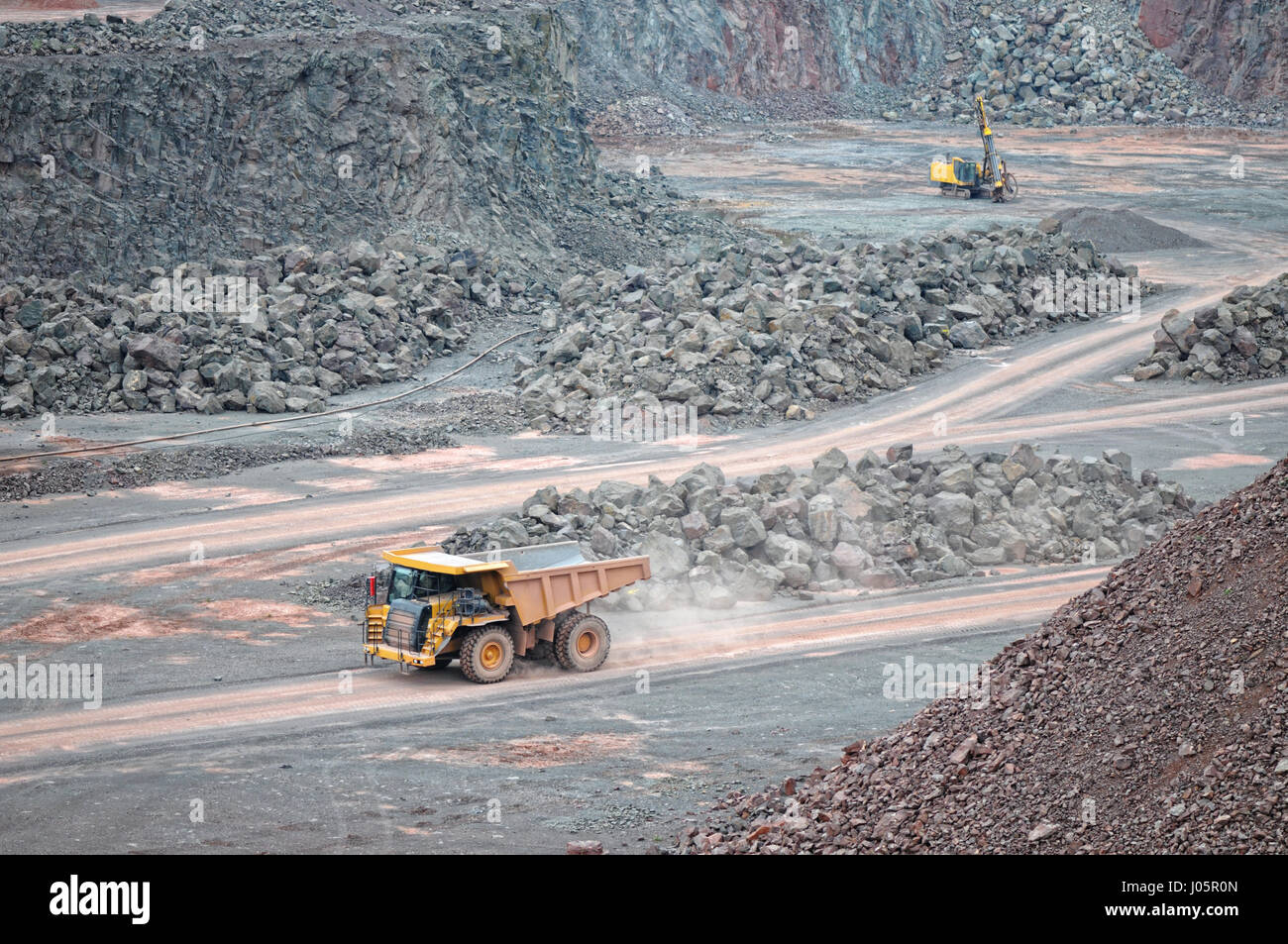 dumper truck driving through a quarry mine. excavator in background ...