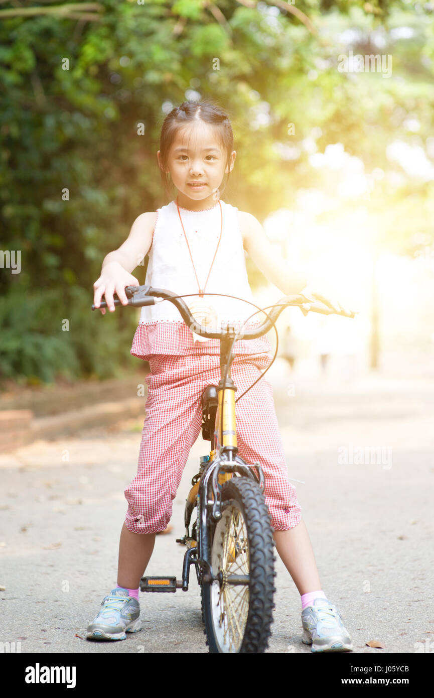 Portrait of active Asian child riding bike outdoors. Little girl having ...