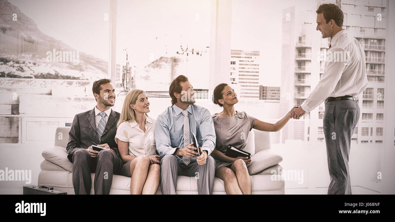 Businessman shaking hand with woman sitting with people waiting for ...