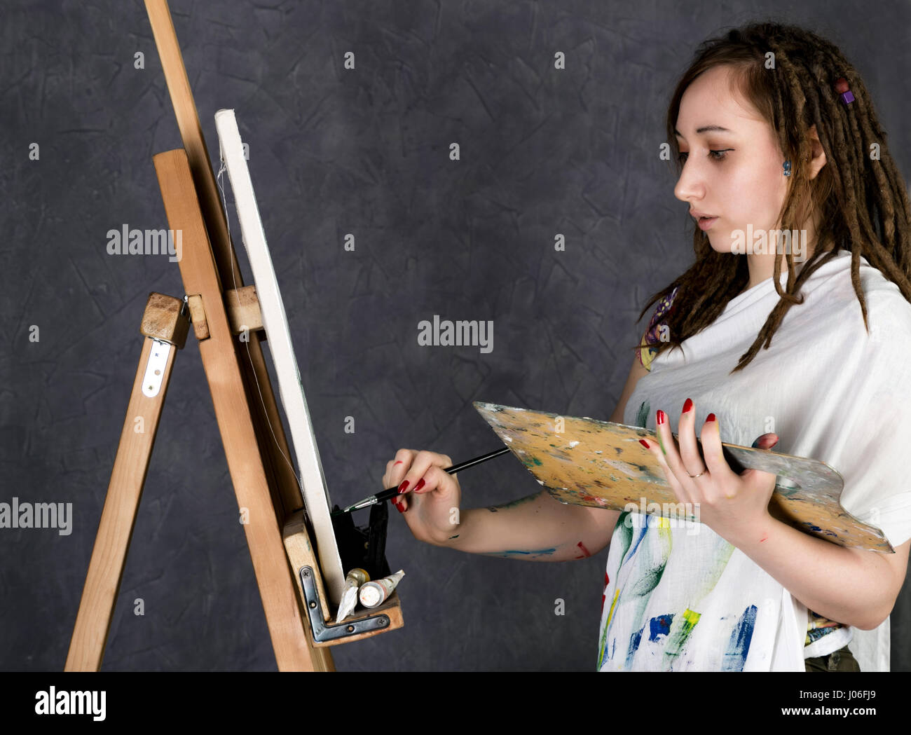 female paint artist posing next to a easel and paints on an canvas ...