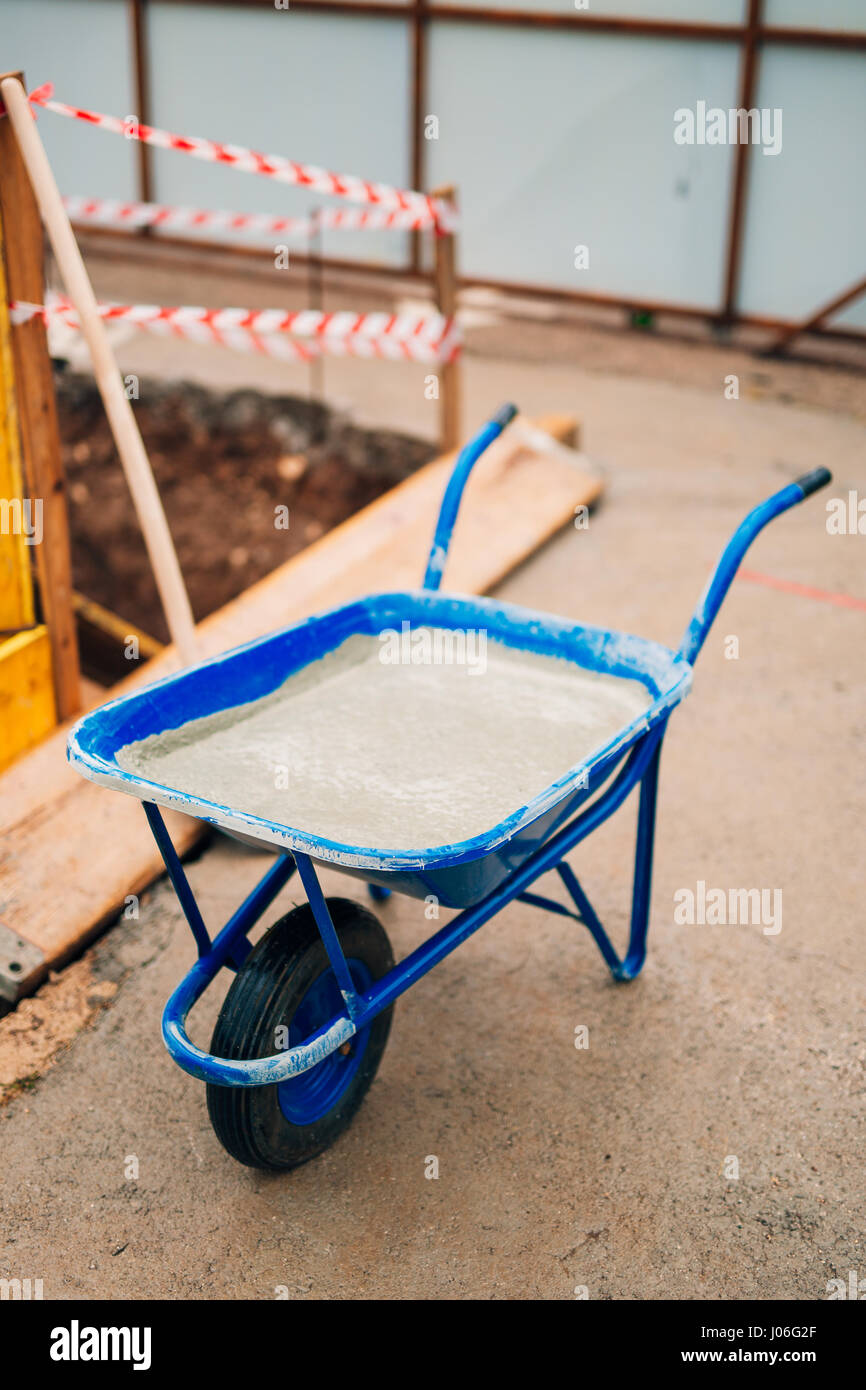 Blue clean new wheelbarrow for cement. Laying the first shovel cement ...