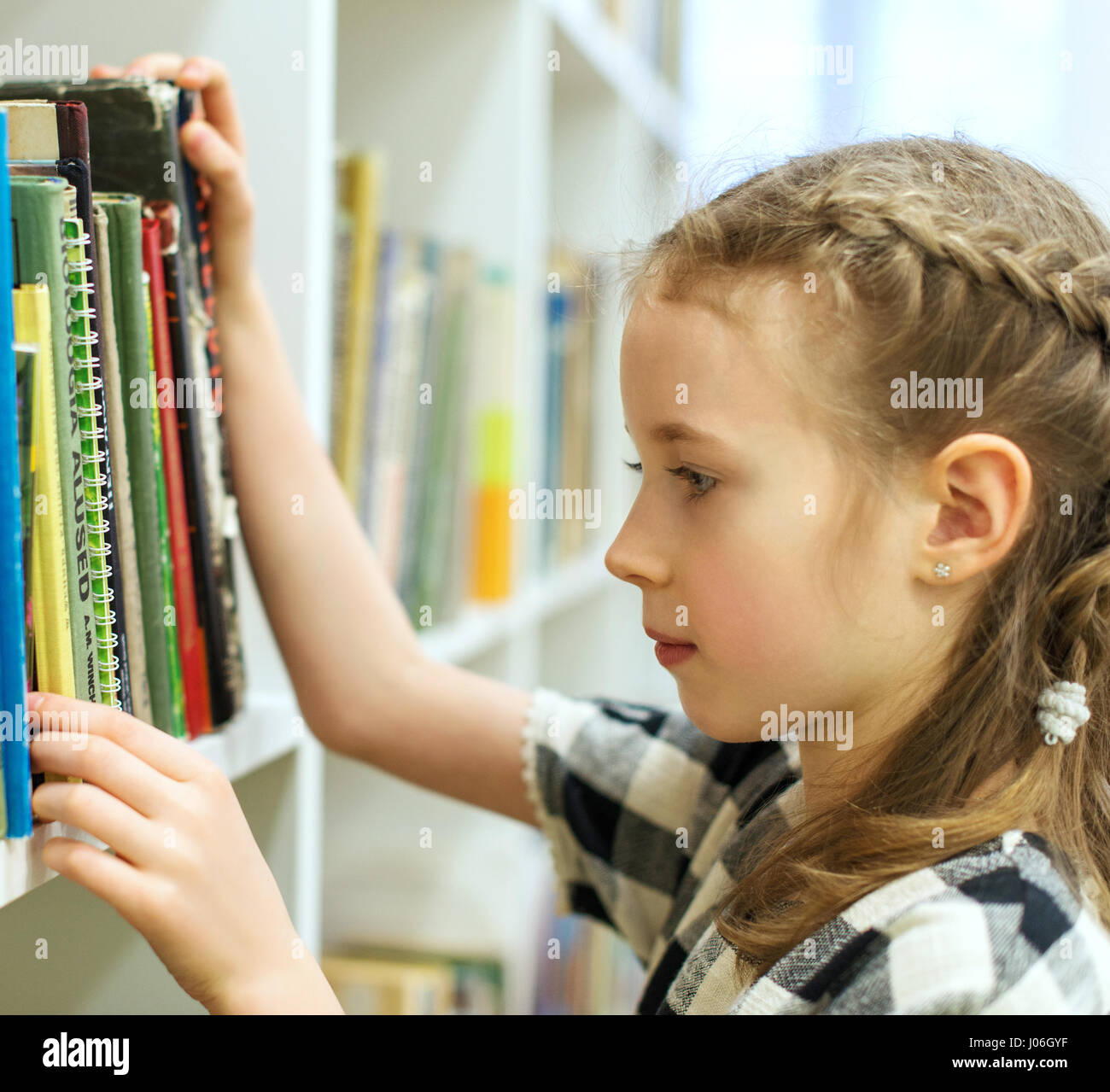 Pretty little girl looking for a book in library Stock Photo - Alamy