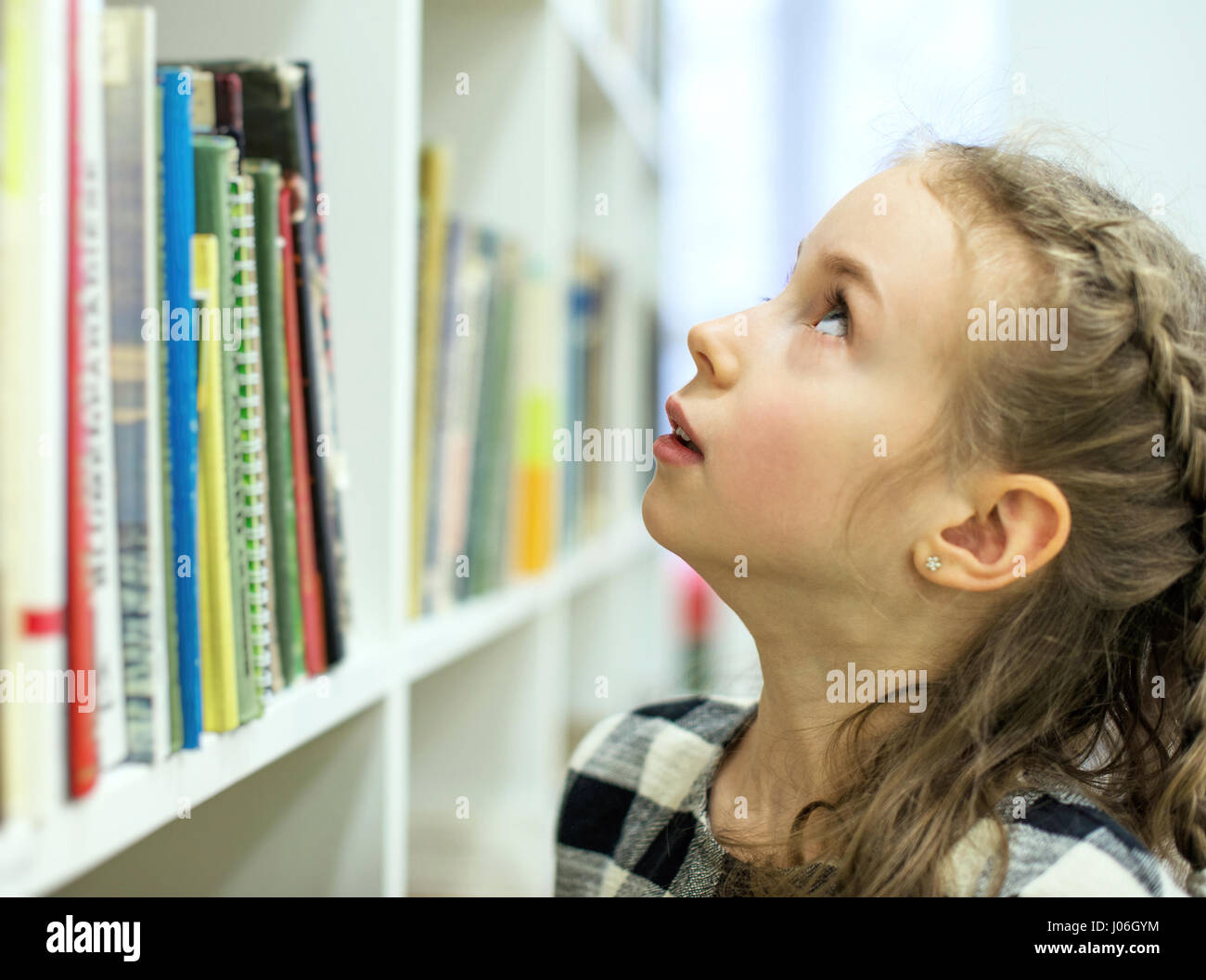 Pretty little girl looking for a book in library Stock Photo - Alamy