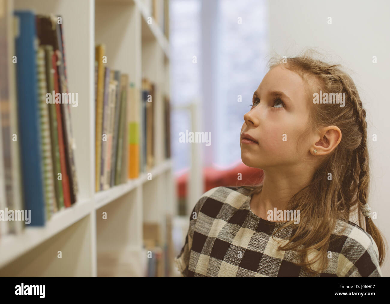 Pretty little girl looking for a book in library Stock Photo - Alamy