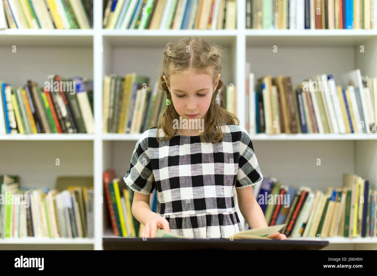Pretty little girl reading a book in library Stock Photo - Alamy