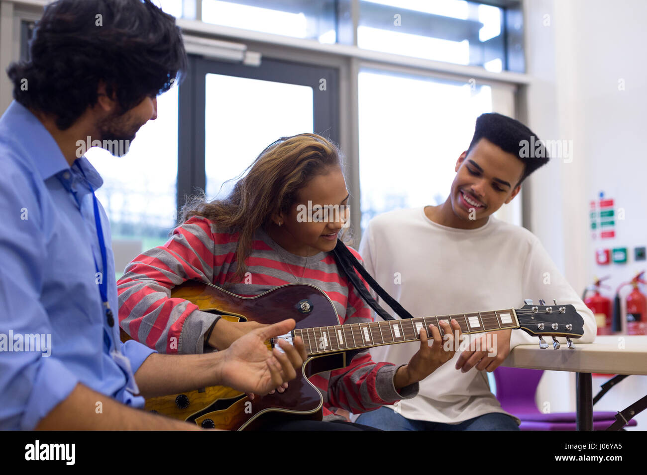 Music teacher helping students learn to play guitar Stock Photo - Alamy