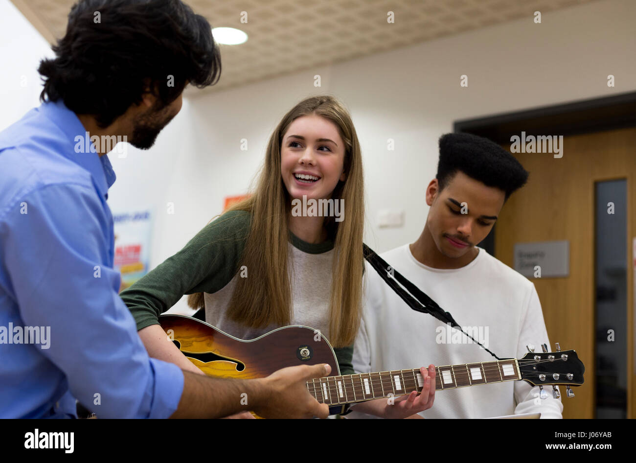 Music teacher helping students learn to play guitar Stock Photo - Alamy