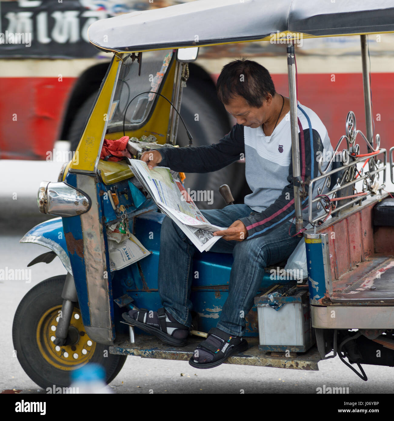 Auto rickshaw driver reading a newspaper at roadside, Bangkok, Thailand ...