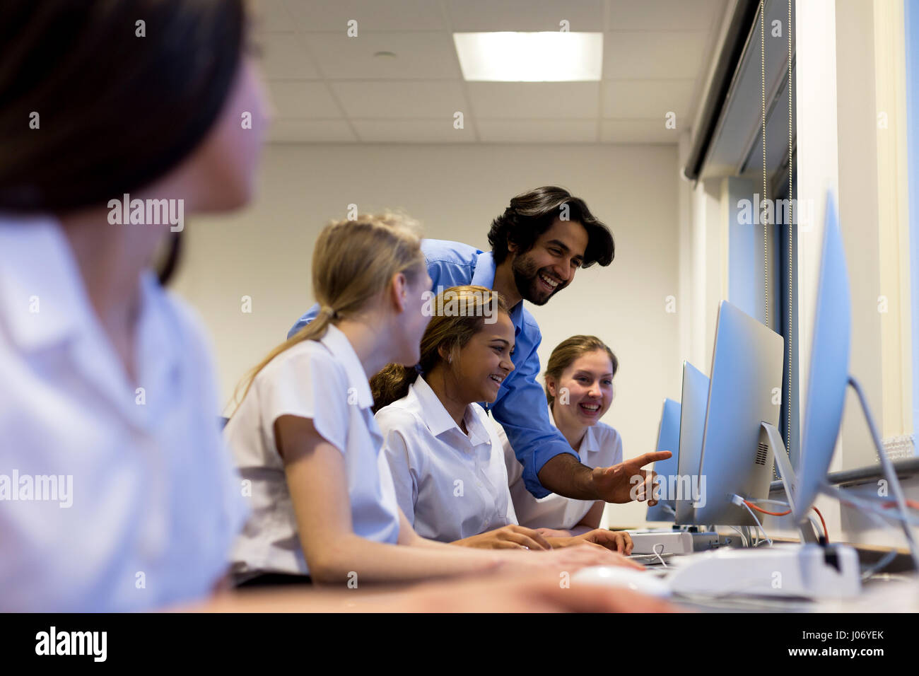 Teacher with students in a computer lesson. They are all looking at a ...
