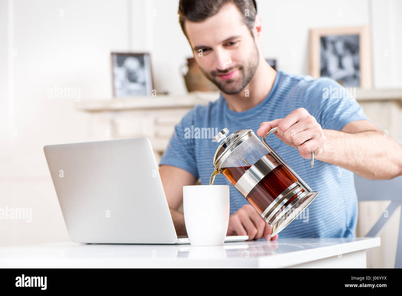 Young smiling man pouring tea in white cup while using laptop Stock ...