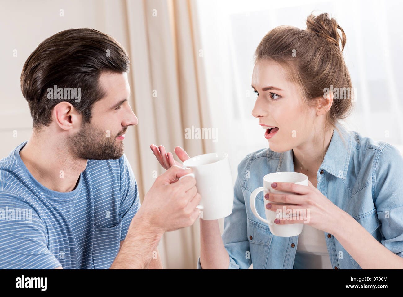 Excited young couple drinking tea from white cups and talking Stock ...