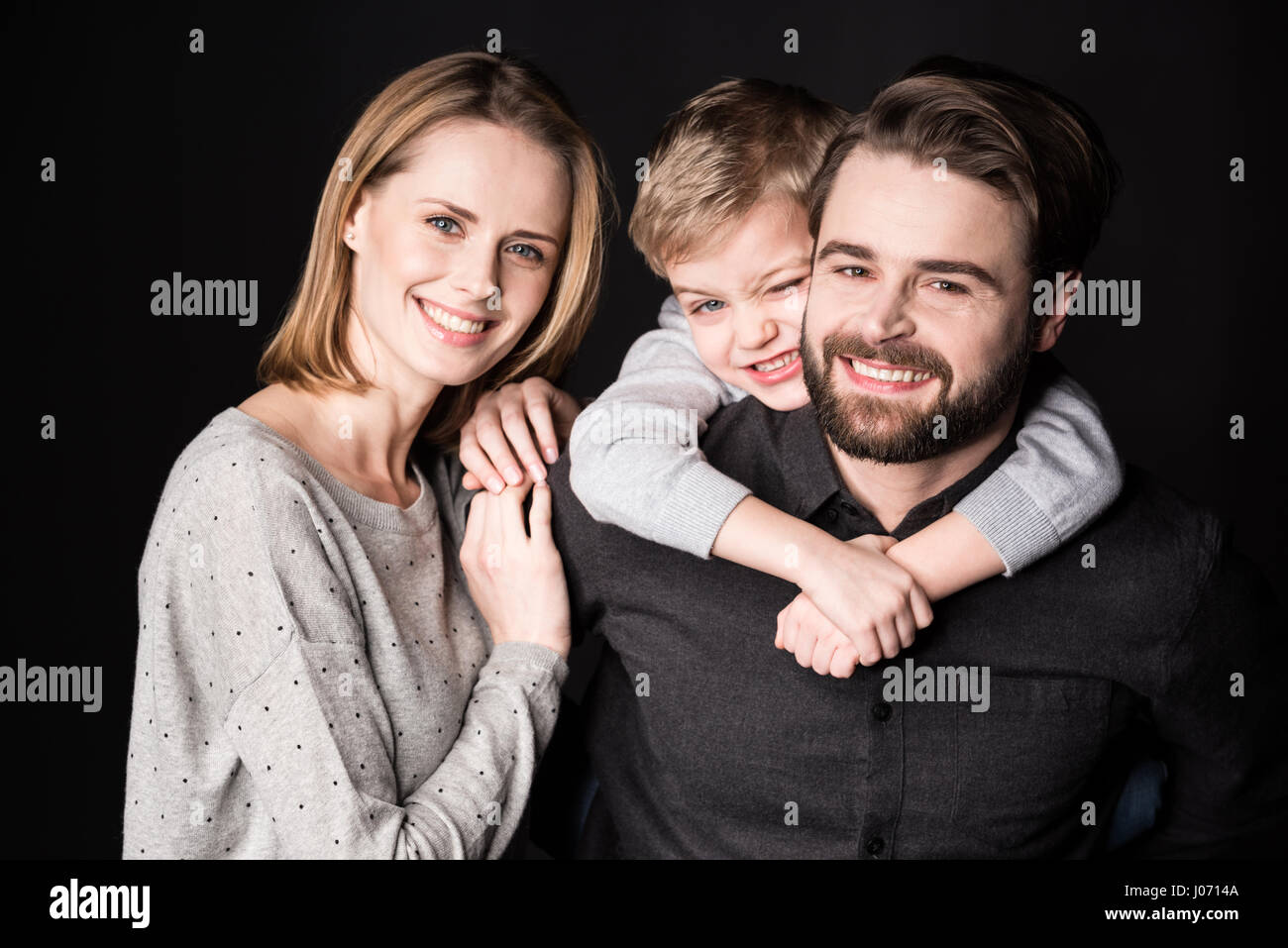 Happy parents with cute little son embracing and smiling at camera on ...