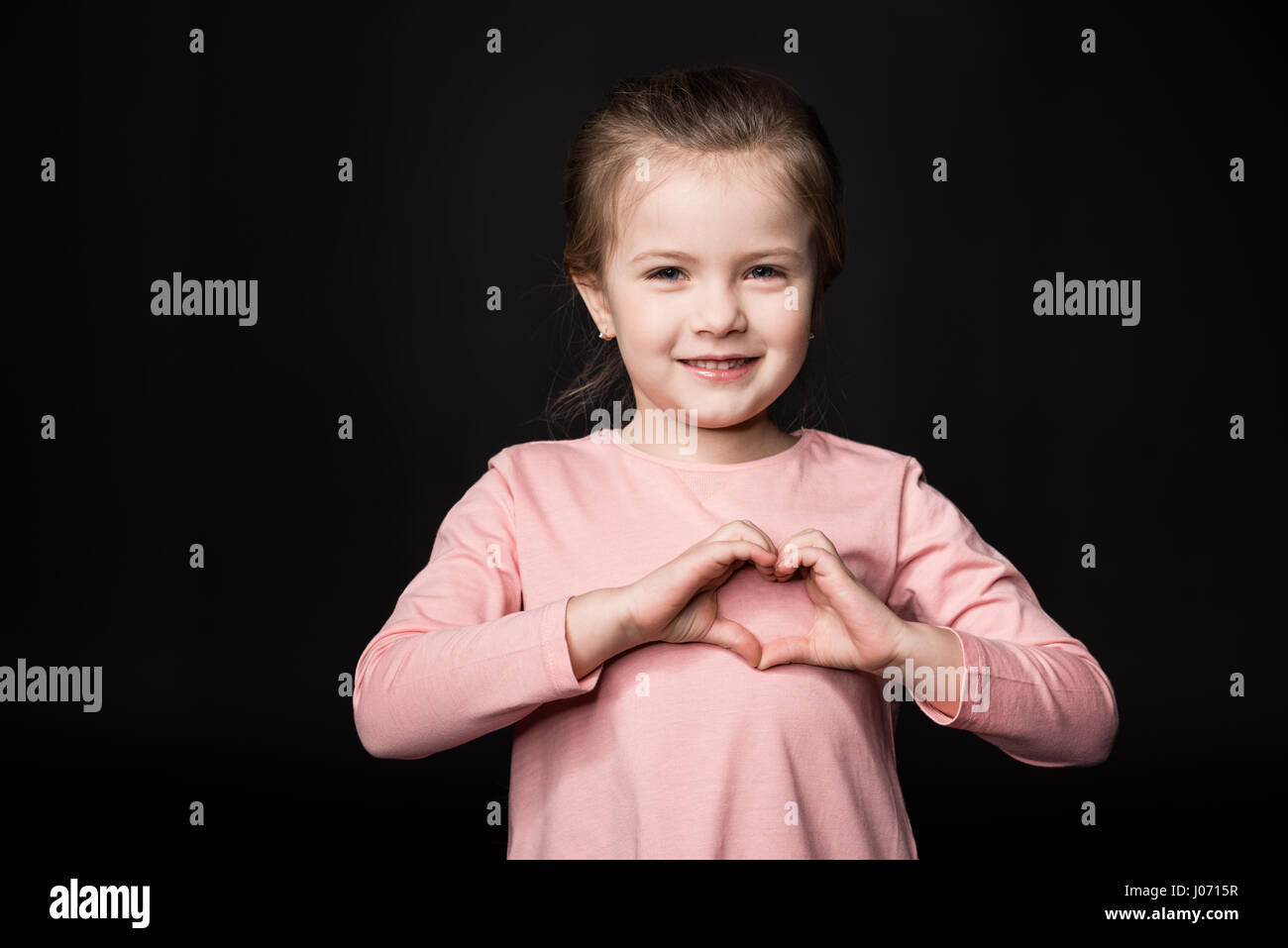 Cute little girl showing heart sign on black Stock Photo - Alamy