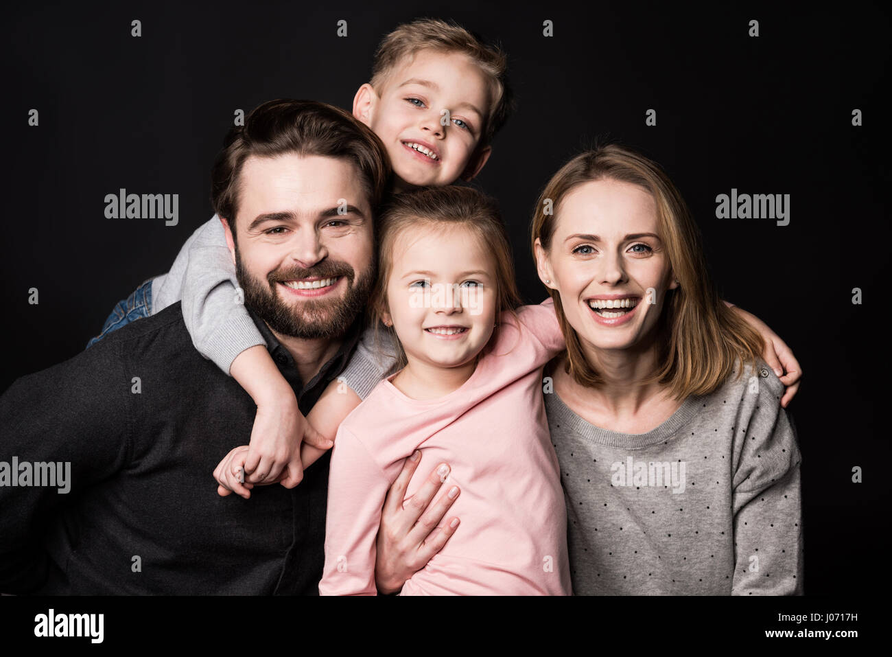 Happy young family standing together and smiling at camera on black ...