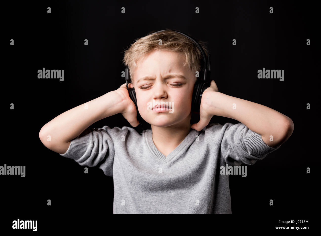 Upset little boy with closed eyes wearing headphones on black Stock ...