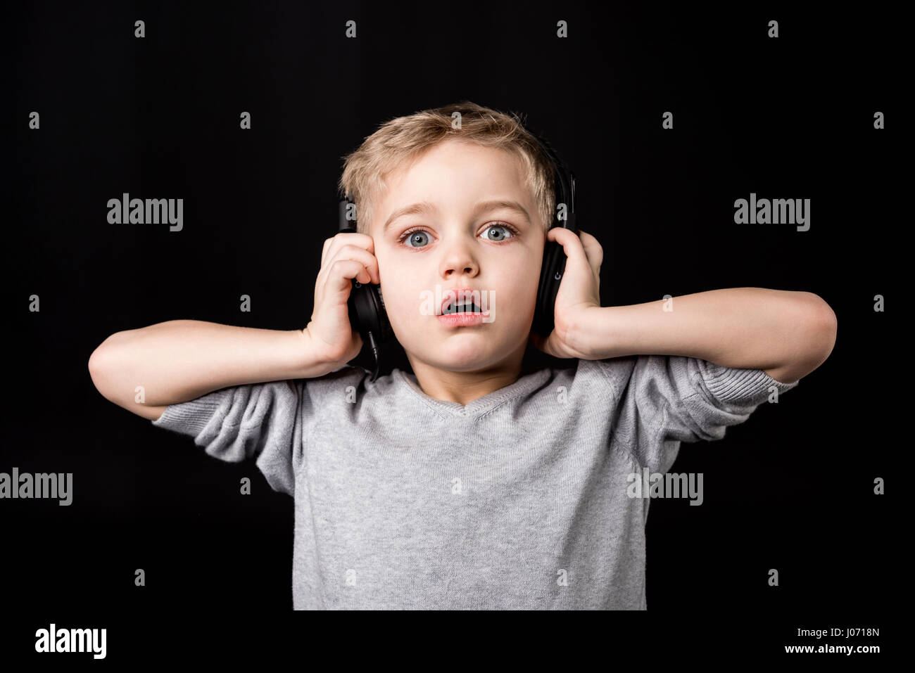 Shocked little boy in headphones looking at camera on black Stock Photo ...