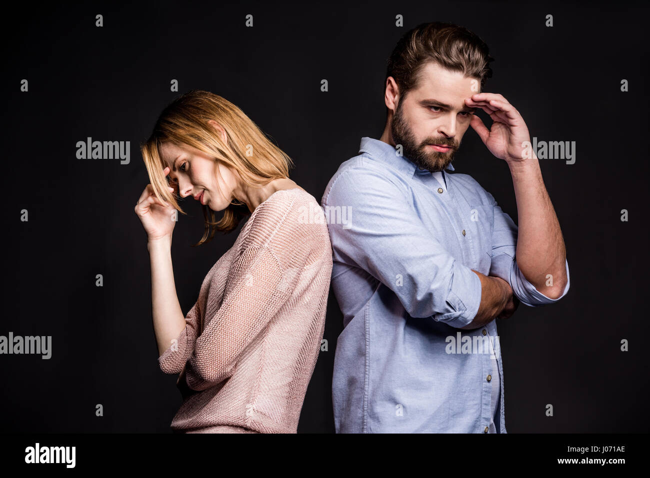 Young man and woman disappointed standing back to back on black Stock ...