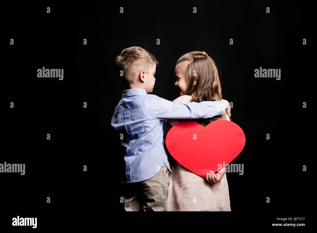 Rear view of little boy hugging little girl who holding red paper heart ...